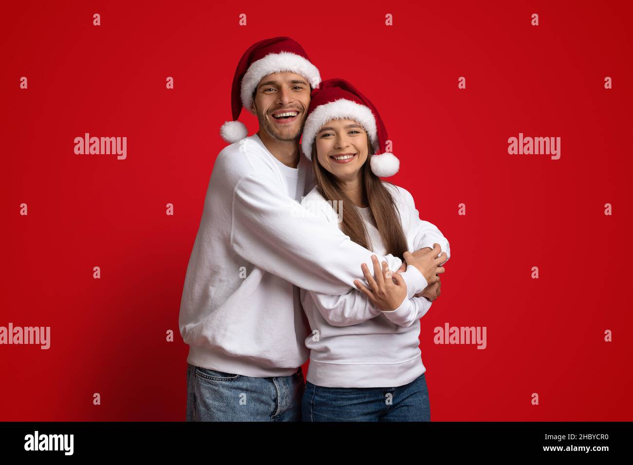 Xmas Romance. Loving Young Couple Wearing Santa Hats Embracing On Red ...