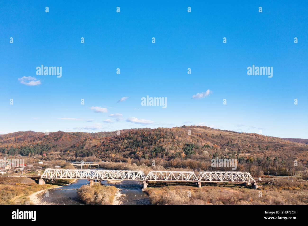 Long railroad bridge over narrow shallow river leading to mountain ...