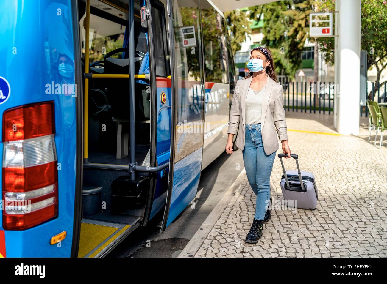 Young woman with luggage and protective mask boarding to the bus in ...