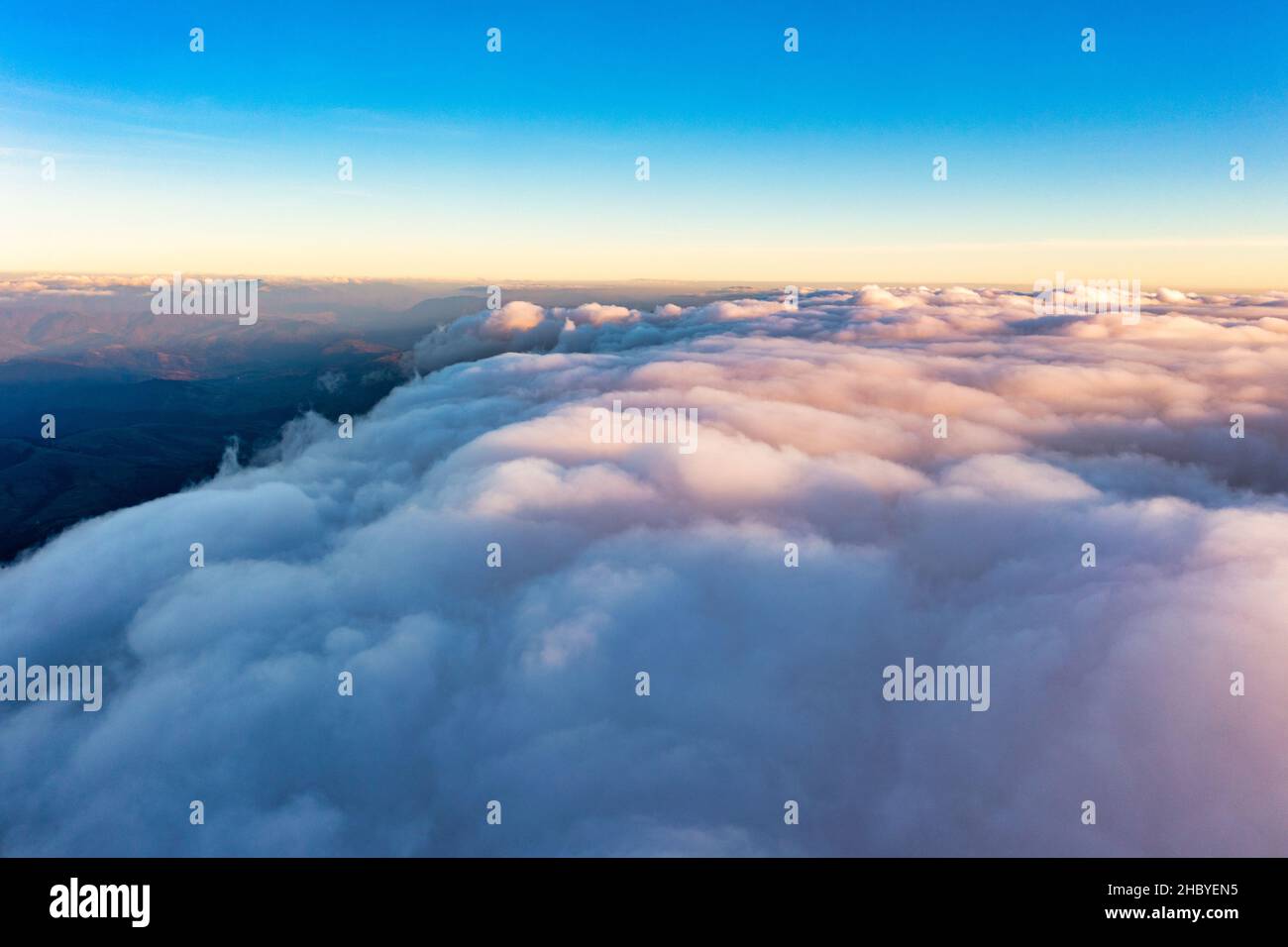 Blue sky above thick layer of white fluffy clouds at bright orange ...