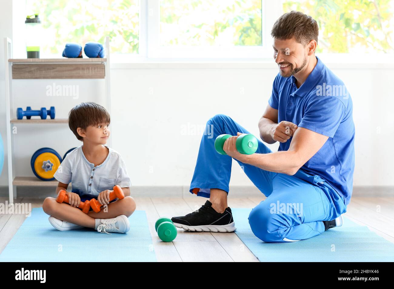 Male coach with dumbbell training little boy in gym Stock Photo - Alamy