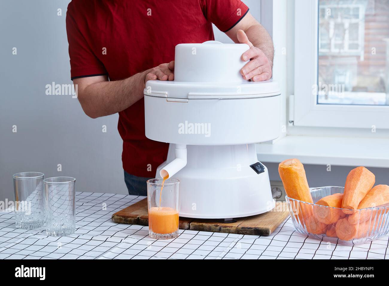 faceless man squeezes carrot juice in a white professional juicer Stock ...