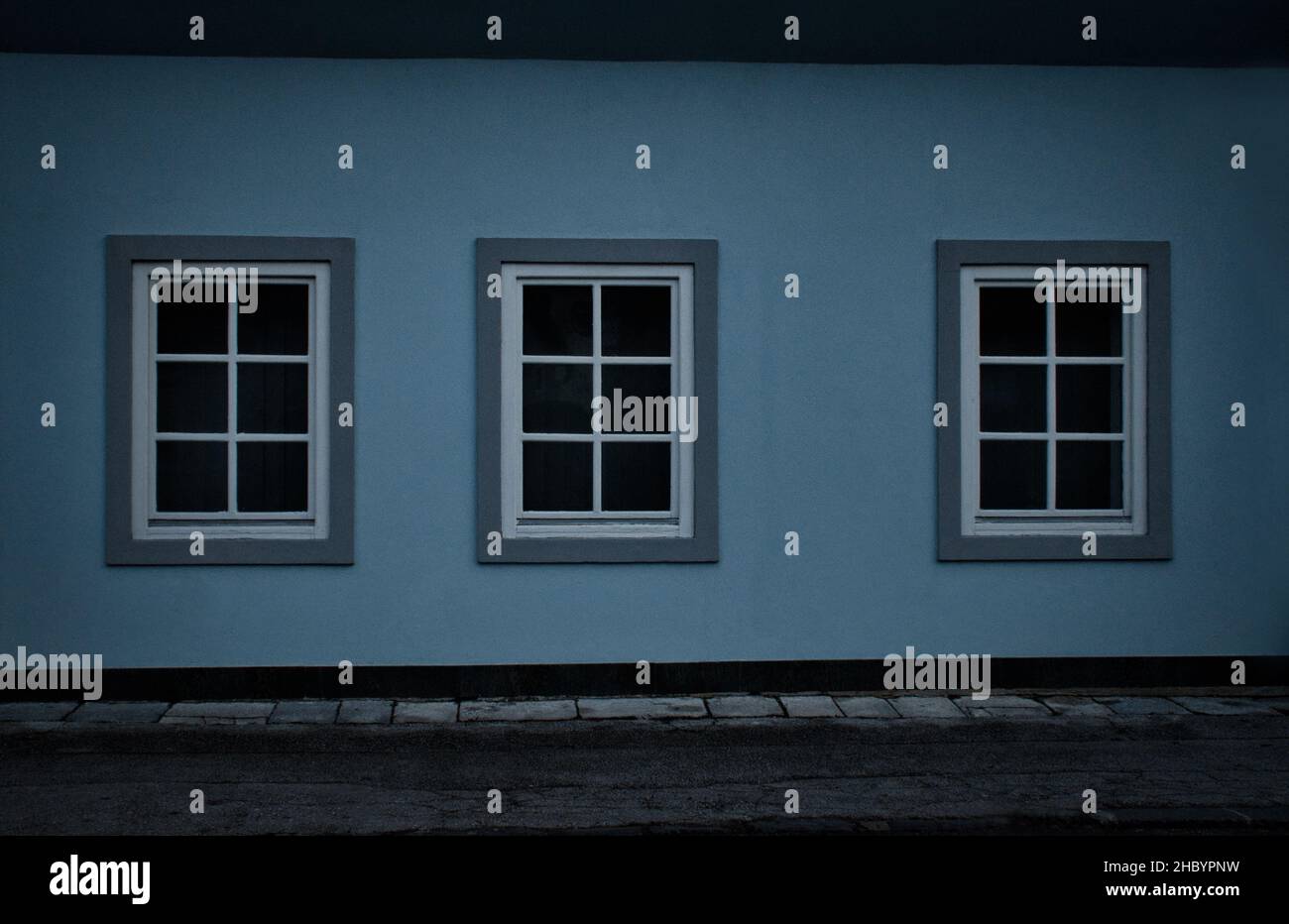 Three windows on a bright blue facade. One window is uneven with other ...