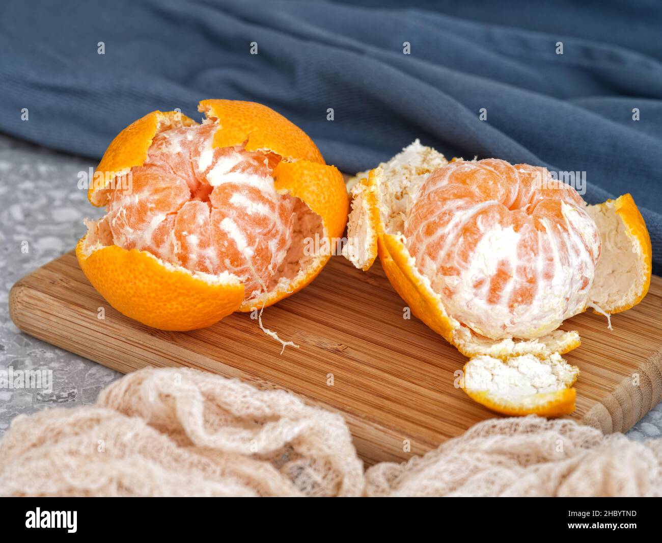 Two peeled tangerines on a cutting board that is on a countertop. Close ...