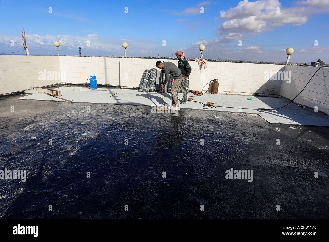 Palestinian workers place tar on the roof of a house to prevent ...