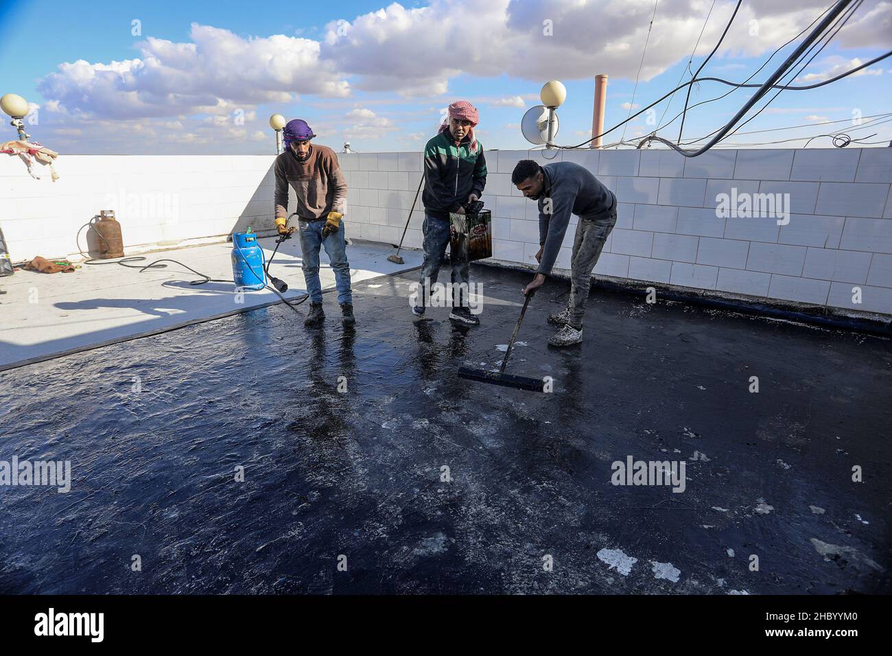Palestinian workers place tar on the roof of a house to prevent ...