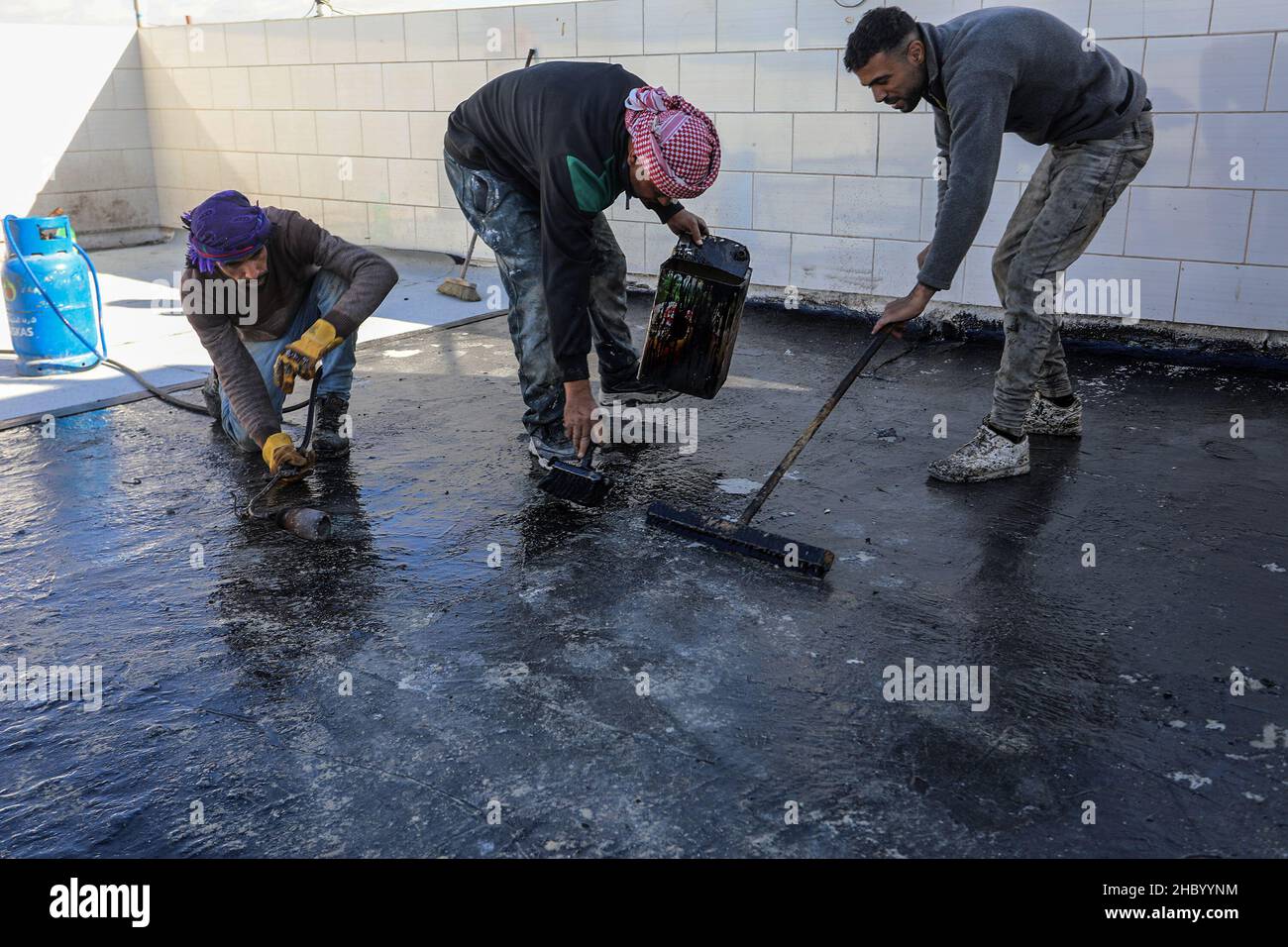 Palestinian workers place tar on the roof of a house to prevent ...