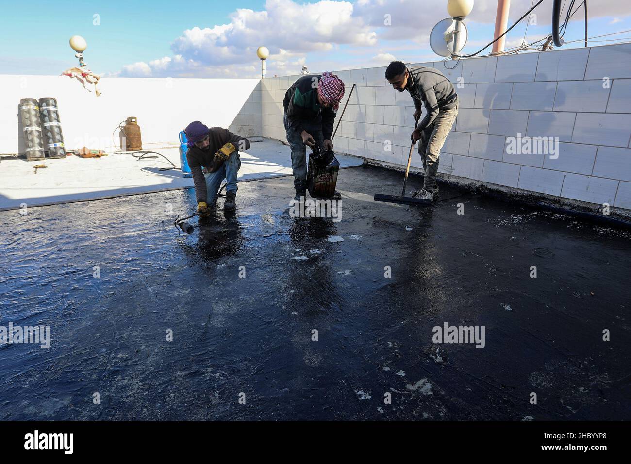 Palestinian workers place tar on the roof of a house to prevent ...