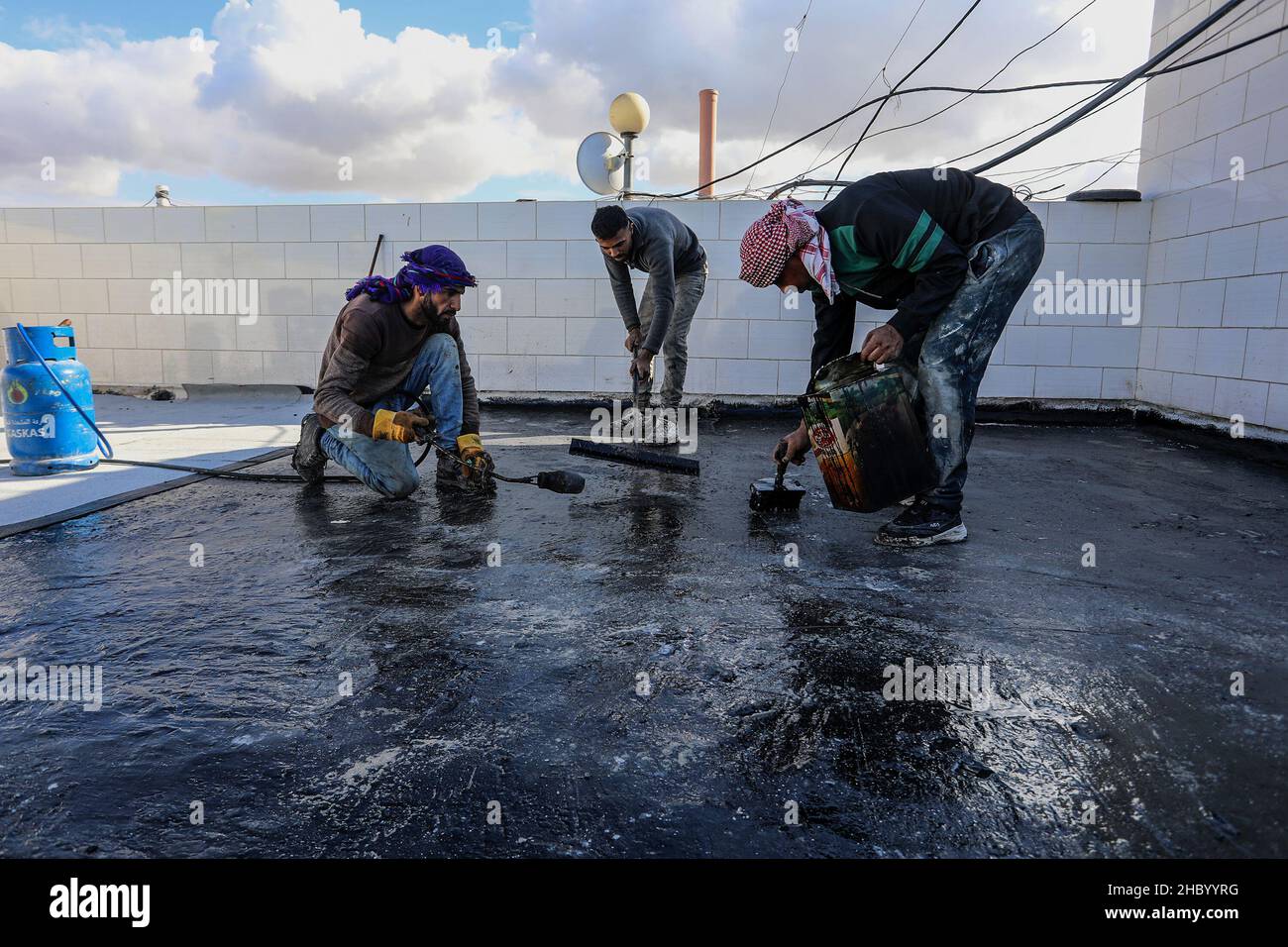 Palestinian workers place tar on the roof of a house to prevent ...