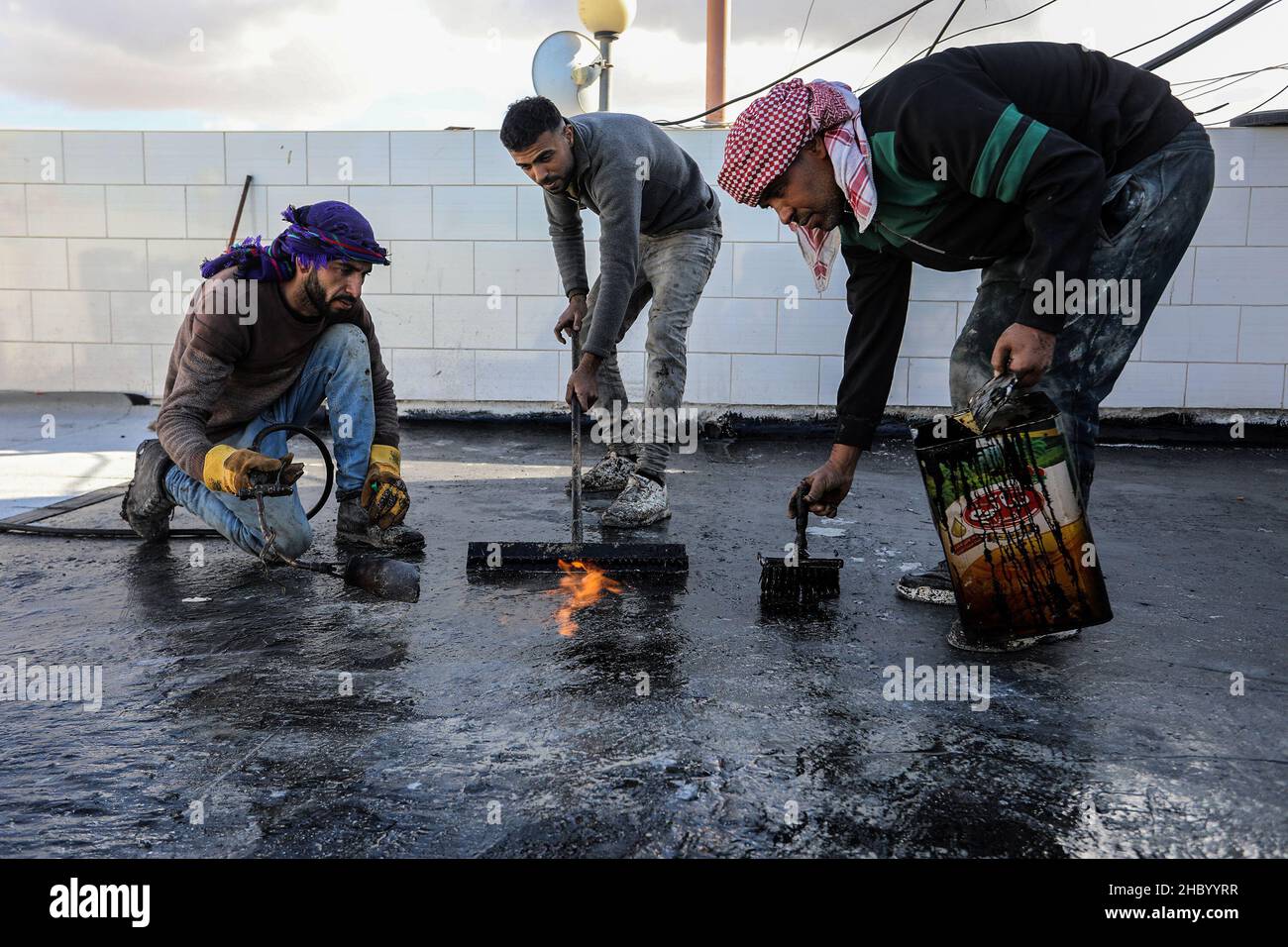 Palestinian workers place tar on the roof of a house to prevent ...