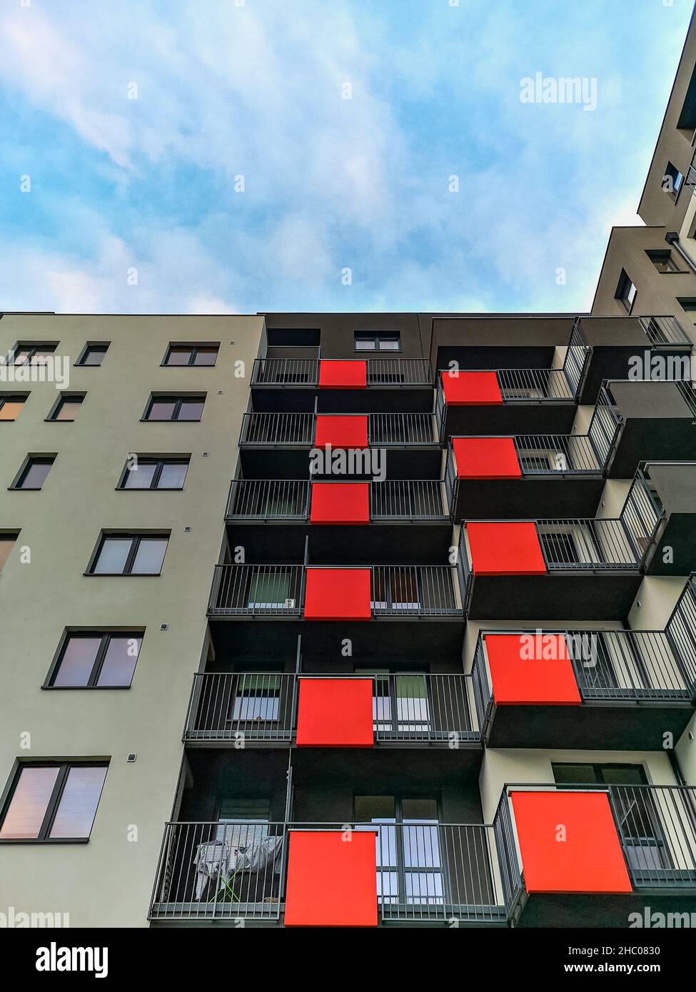 Looking up to facade of modern block of flat with dark balcony with red ...