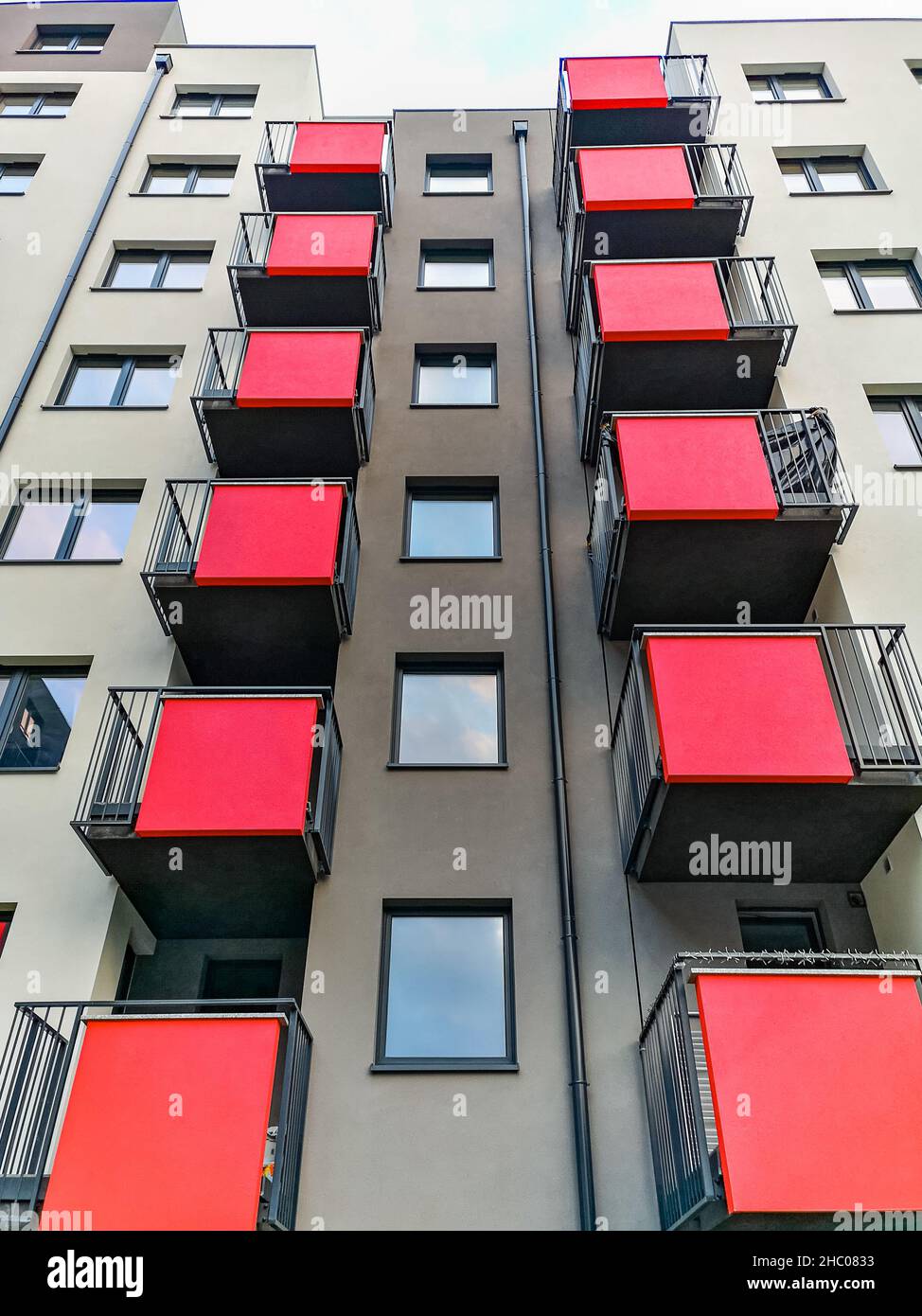 Looking up to facade of modern block of flat with dark balcony with red ...