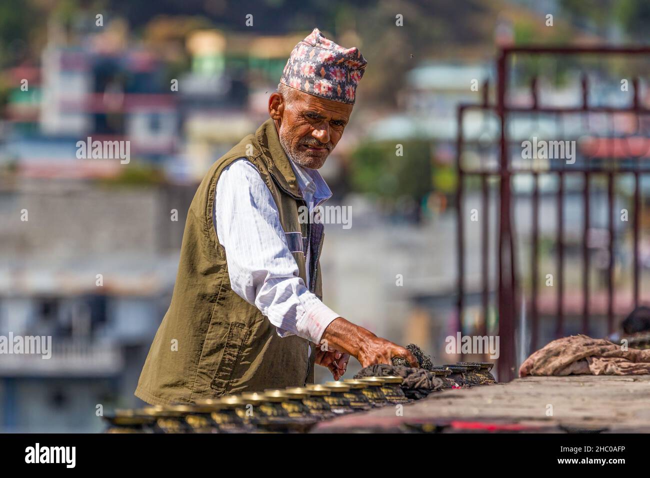 An older Nepali Hindu man in a Dhaka topi cap cleans butter lamps at ...