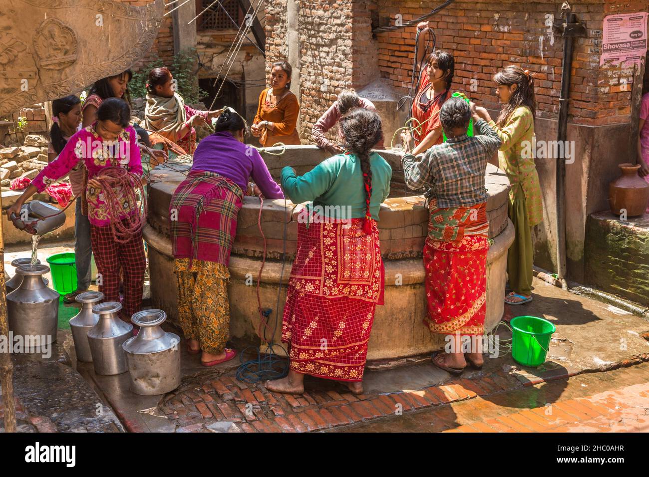 Newari women draw water from a stone water well with buckets on ropes ...