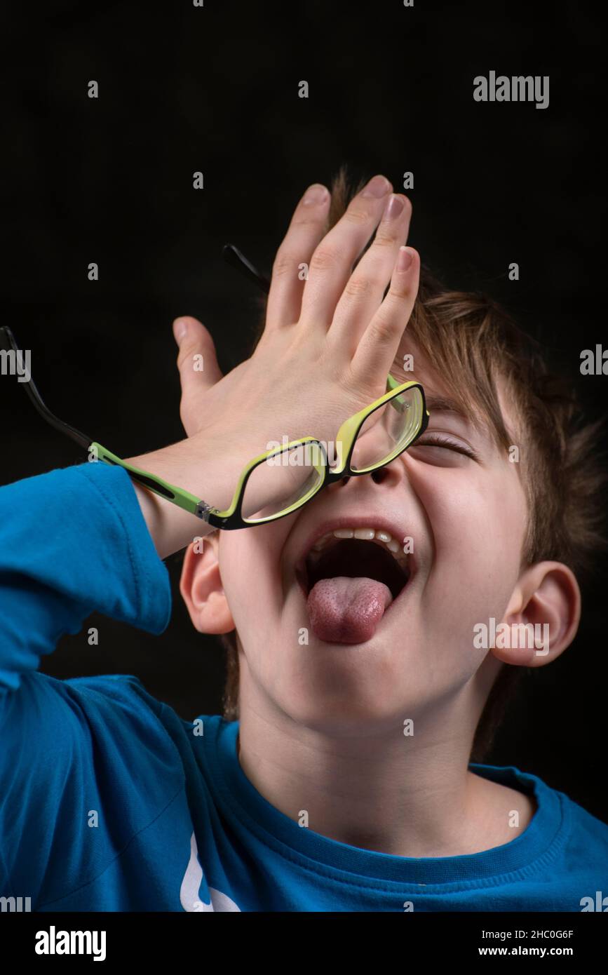 Boy laughs and doing song facepalm. Portrait of fun schoolboy on black ...
