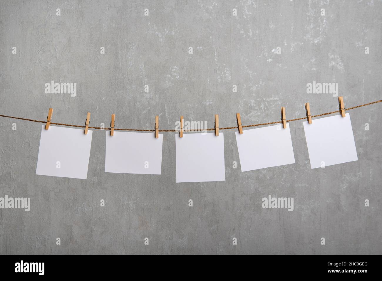 Blank paper notes hang with clothespins on rope. Grey background. Copy ...