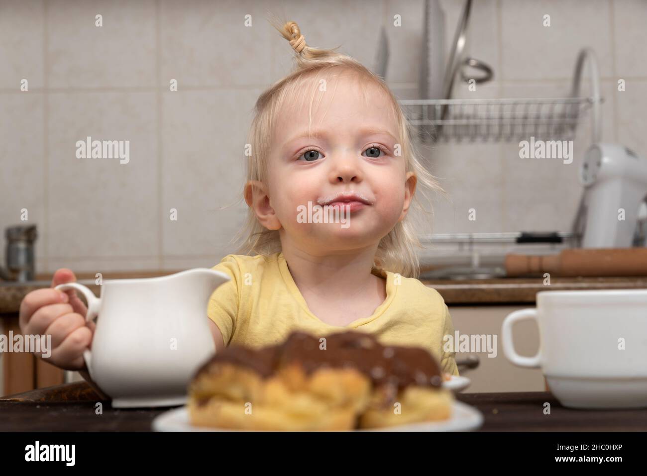 Blonde child is having breakfast in the kitchen. Kid drinking tea ...