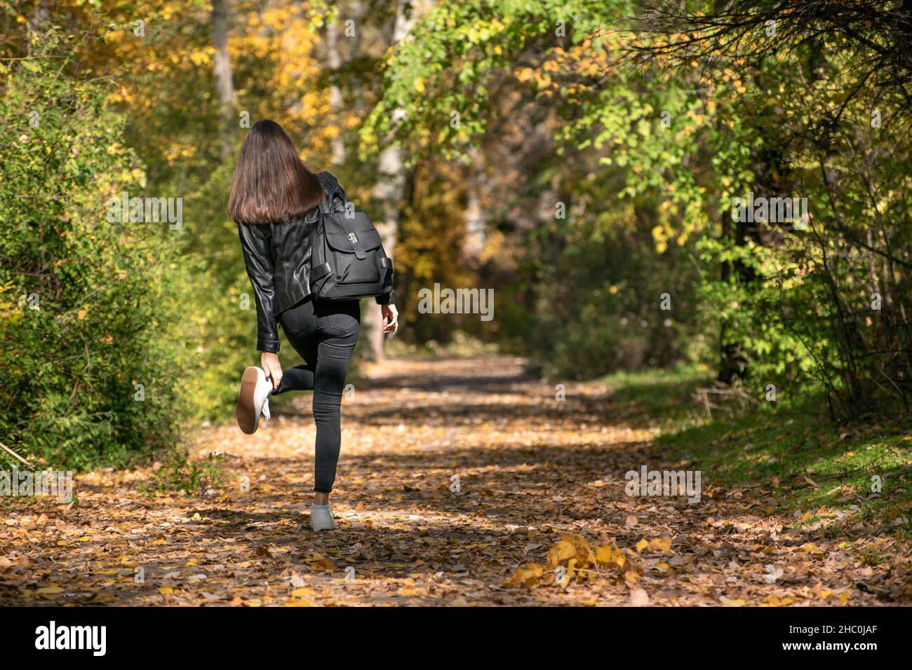 Girl student walks in autumn park. Girl with dark hair straightens her ...