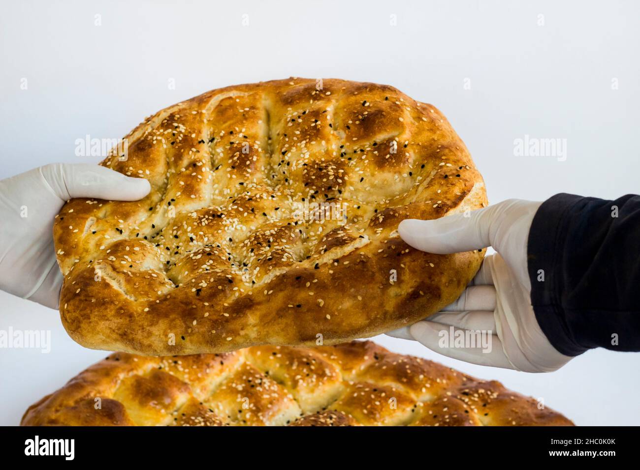 Two hands wearing gloves giving each other Ramadan Bread on white Stock ...