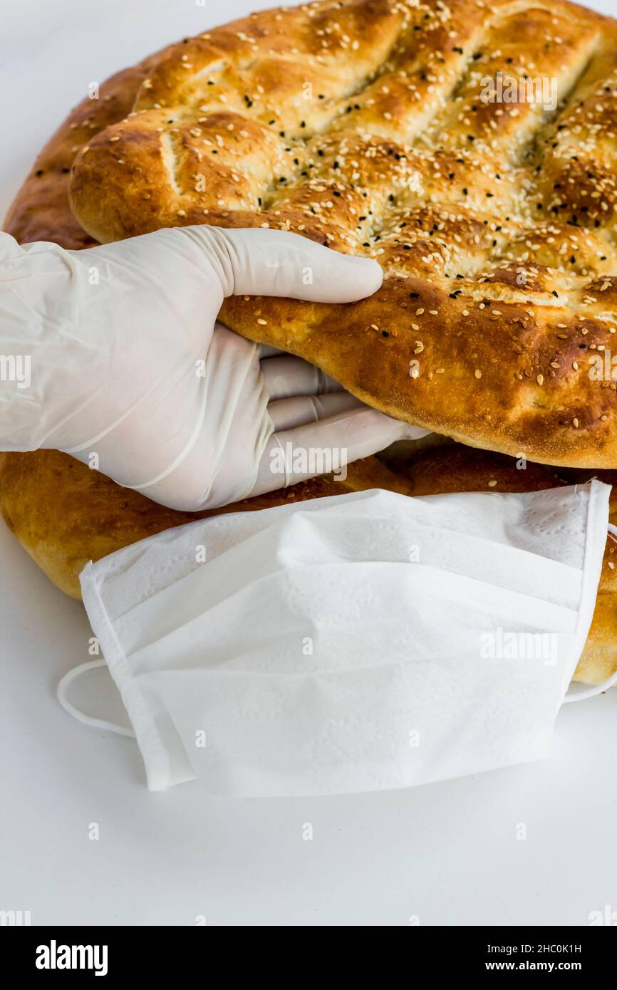 Gloved hand holding ramadan bread with medical face mask on white ...