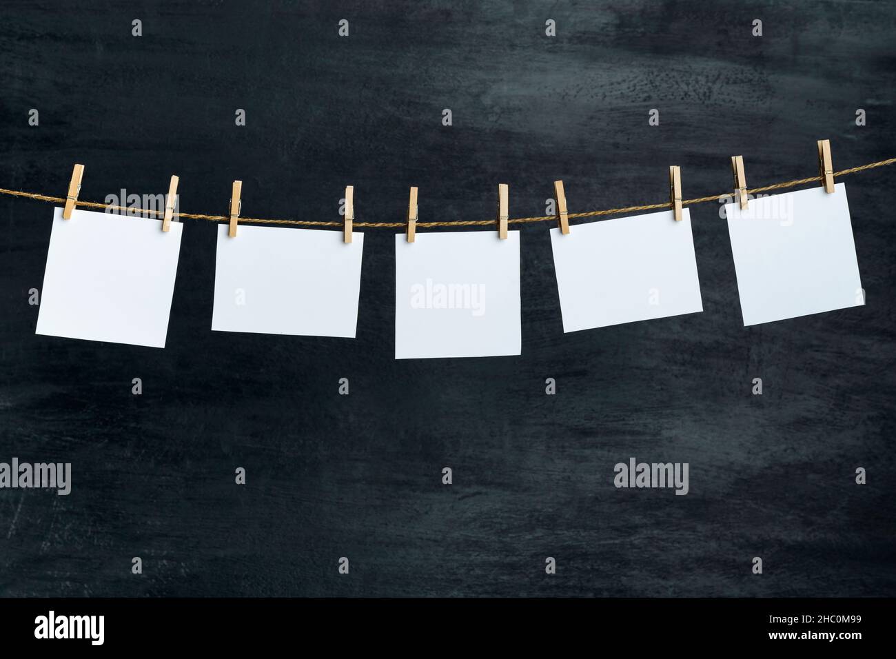 Blank paper notes hang with clothespins on rope. Black background. Copy ...