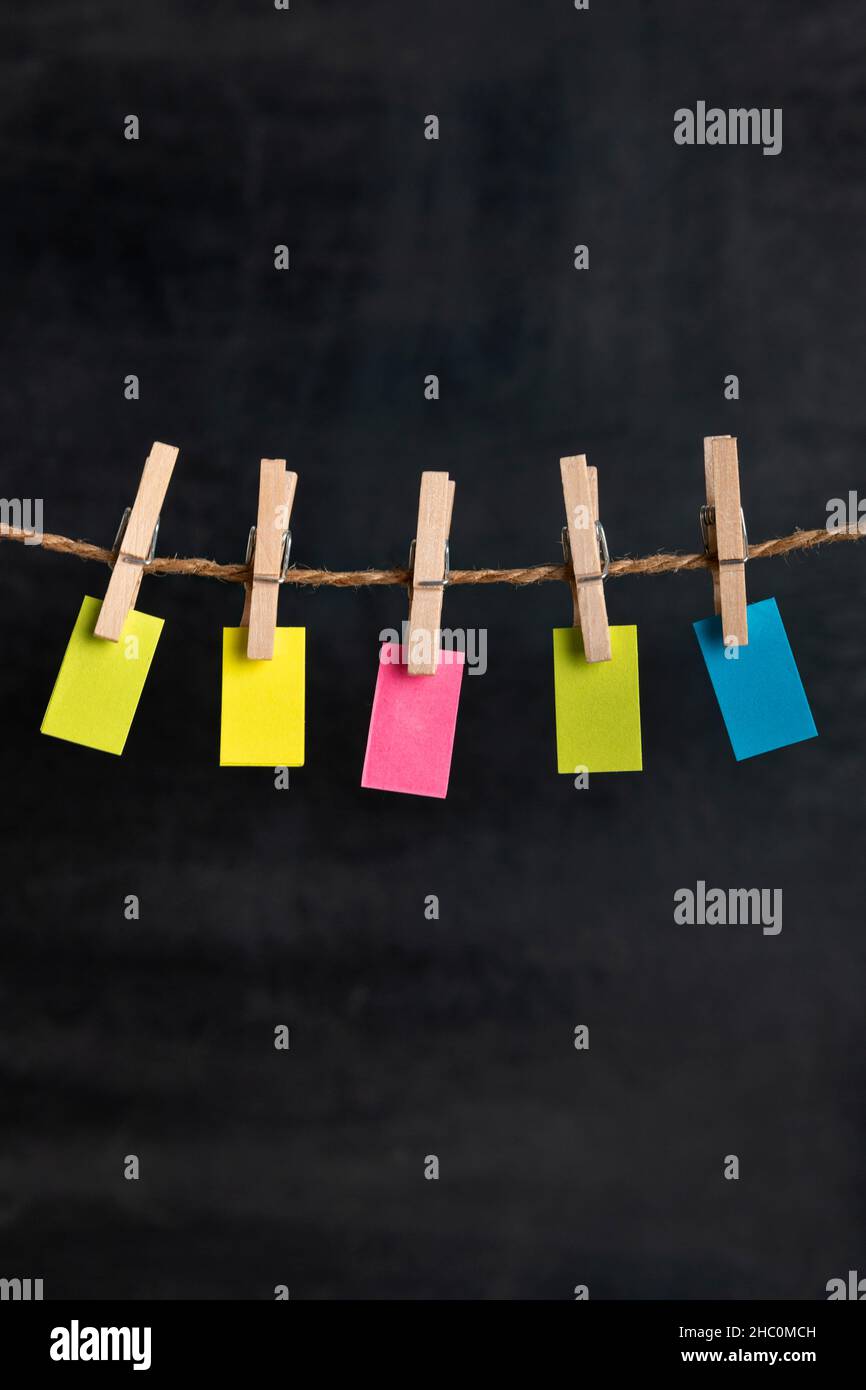 Small bright notes hang with clothespins on rope. Black background ...