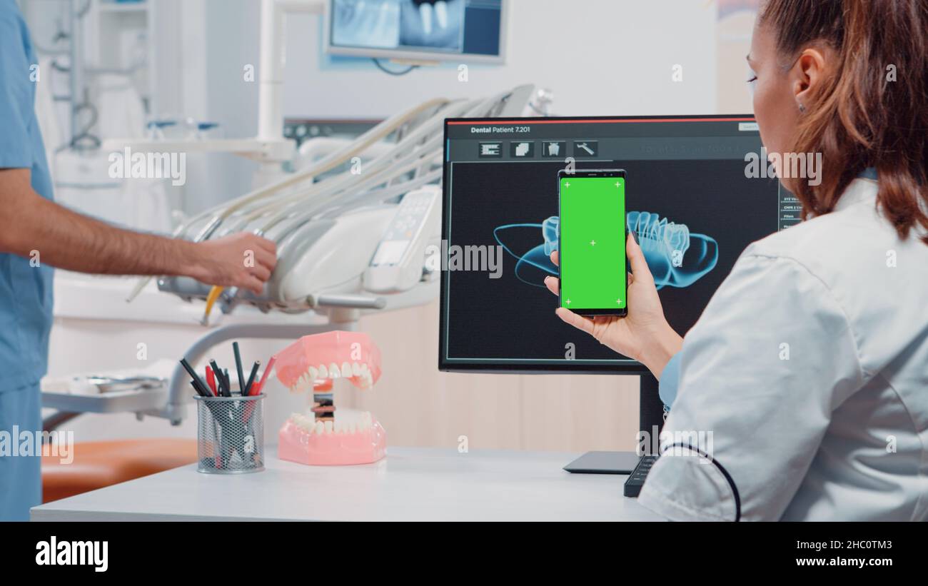 Dentist vertically holding smartphone with green screen while looking ...