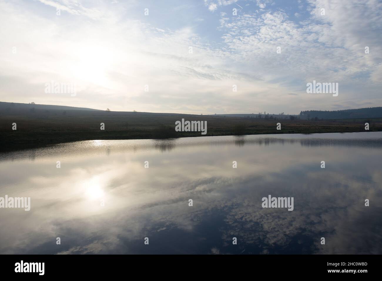 Horizontal wide angle image of a bright winters sky reflected in a calm ...