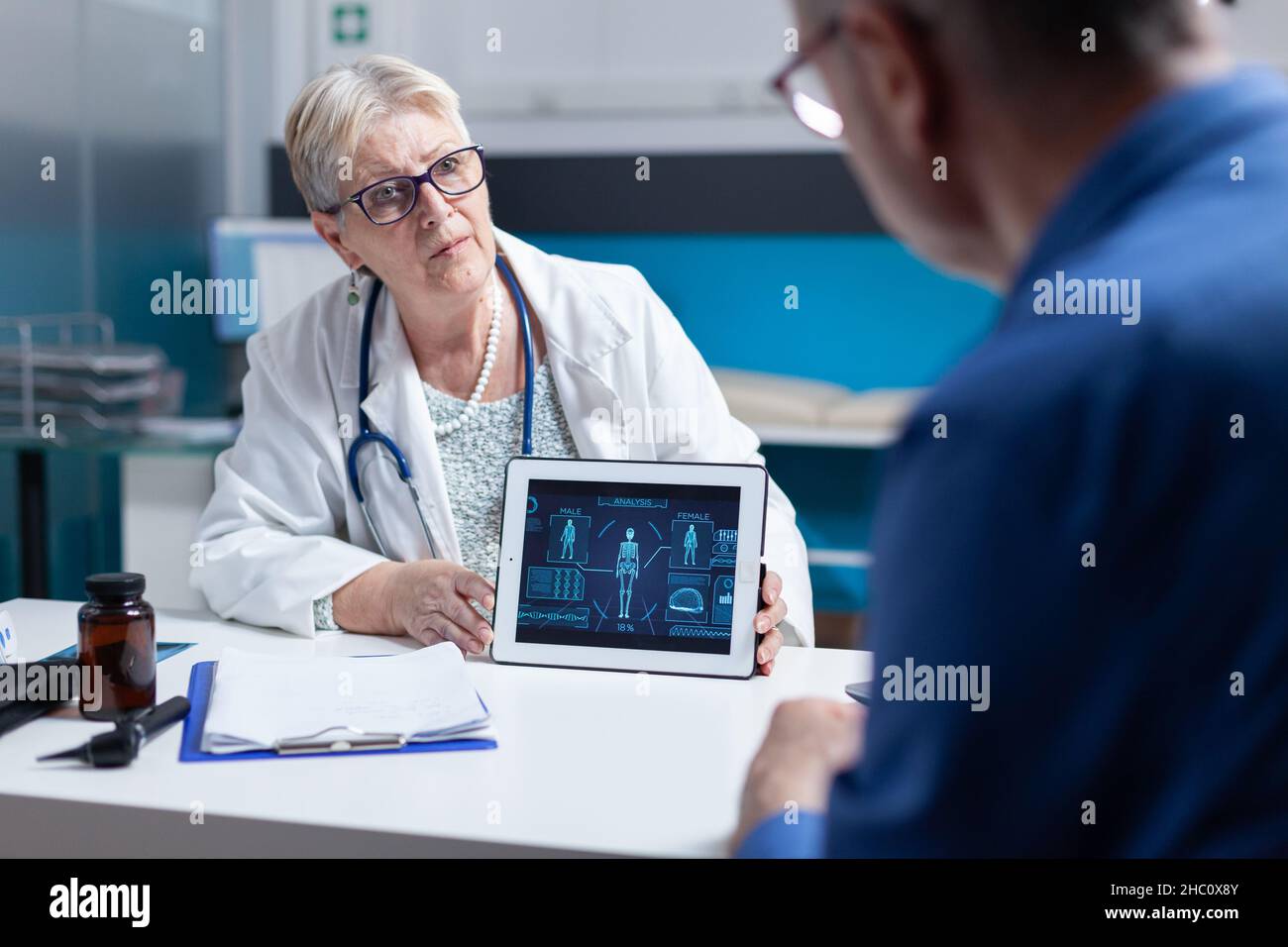 Physician explaining human body analysis on tablet to patient with ...