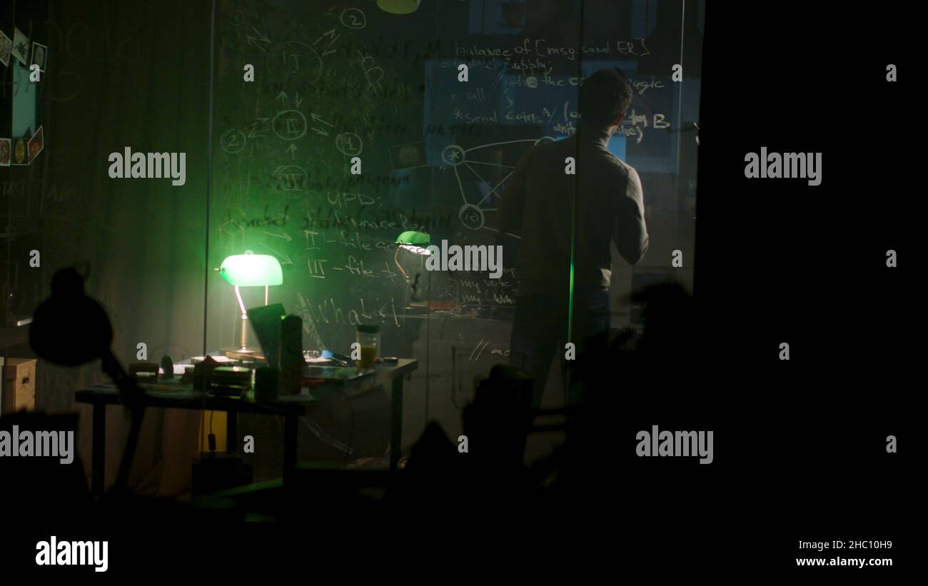 Businessman writing notes on the glass board near the mess on his table ...