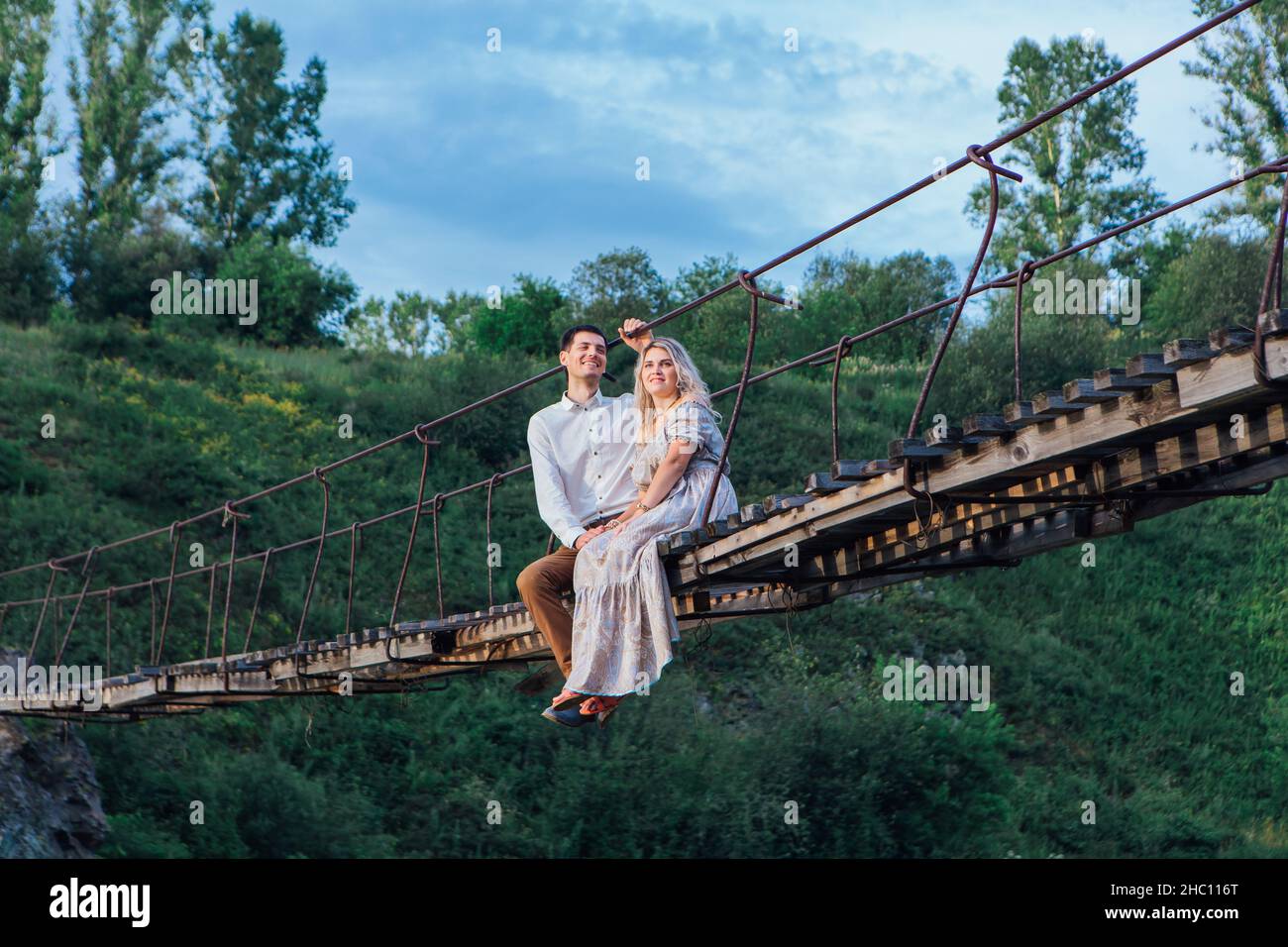 Beautiful young couple sitting on the suspension bridge Stock Photo - Alamy