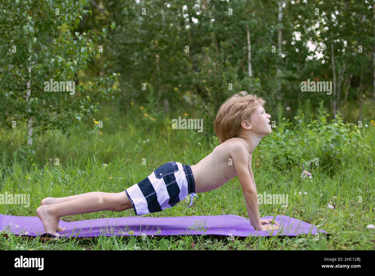 Little boy in striped shorts does plank exercise on fitness mat in park ...