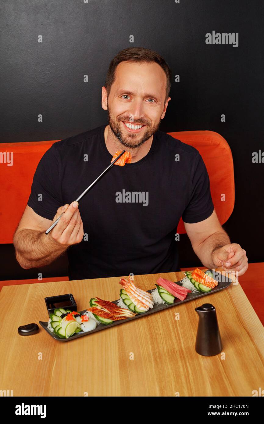 Positive man eating delicious Japanese assorted sashimi set in cafe ...