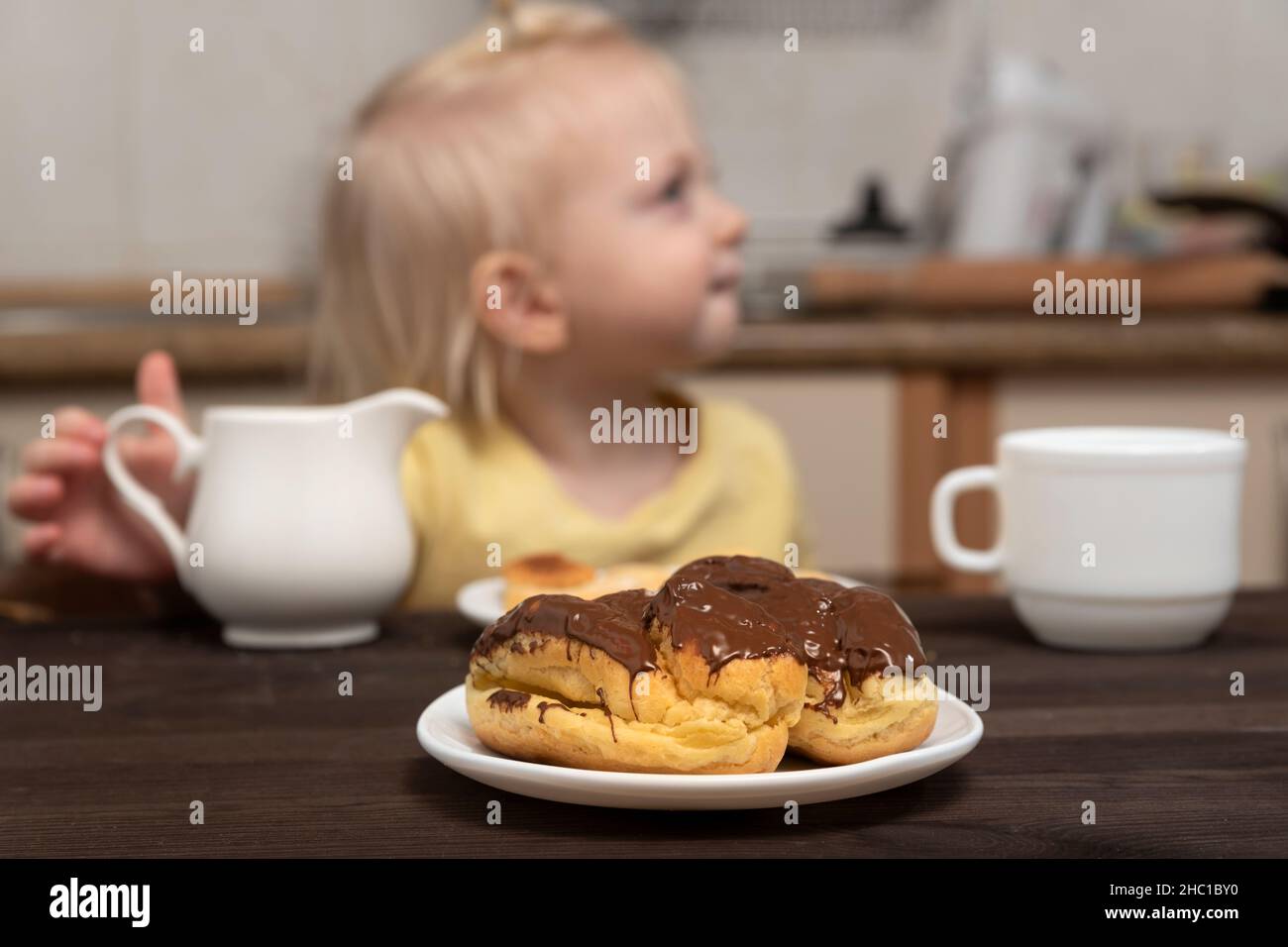 fair-haired child having breakfast in kitchen. Custard cakes on kid ...