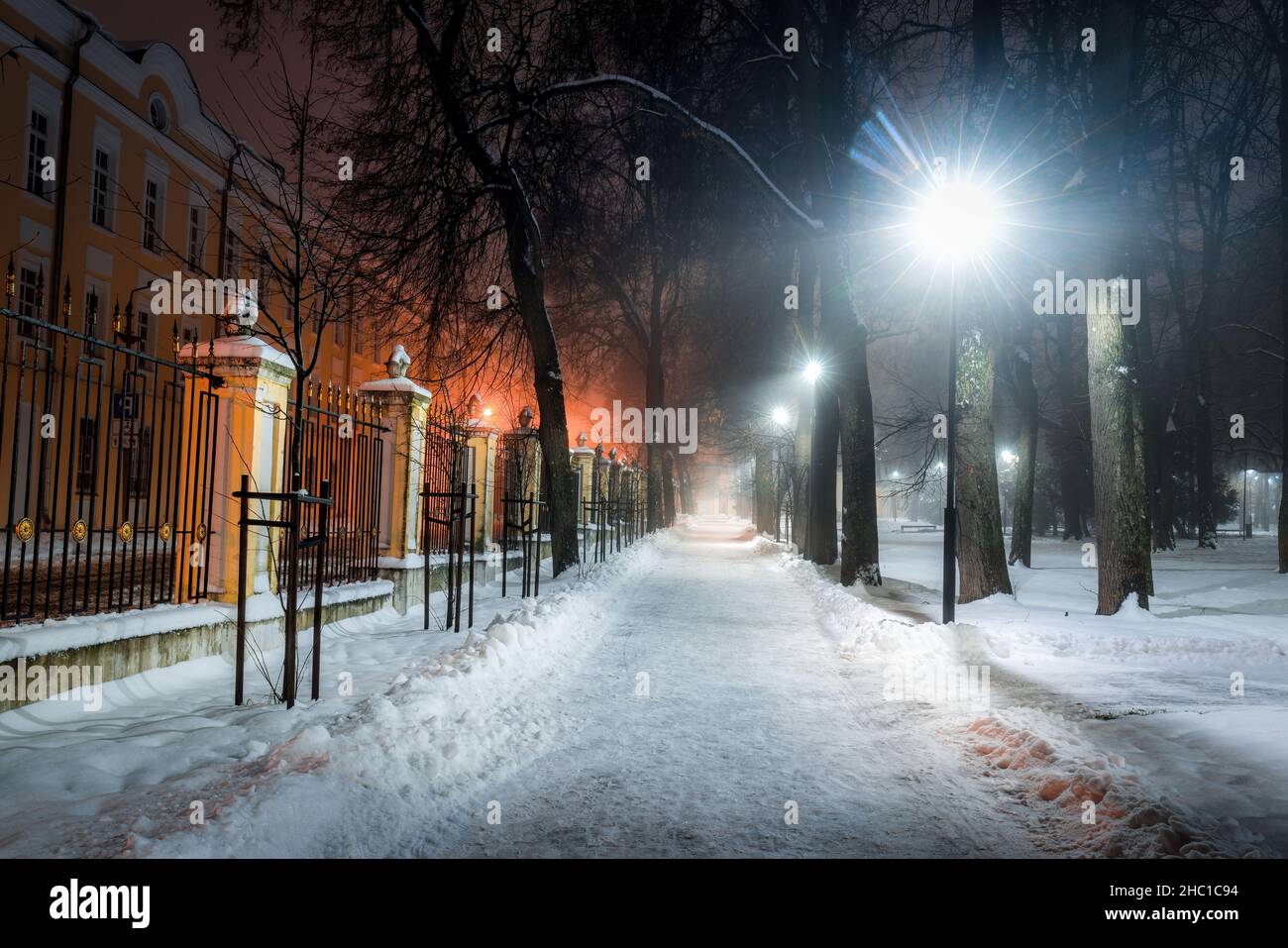 First snow in a winter night park with trees, glowing lanterns and ...