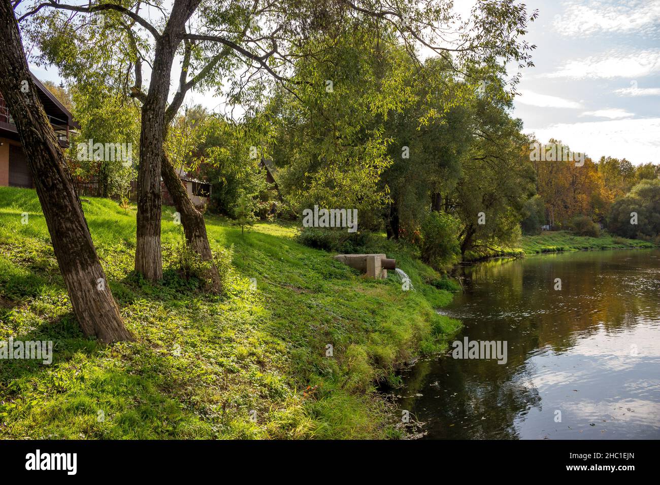 Beautiful landscape with a river bank and water discharge from a pipe ...