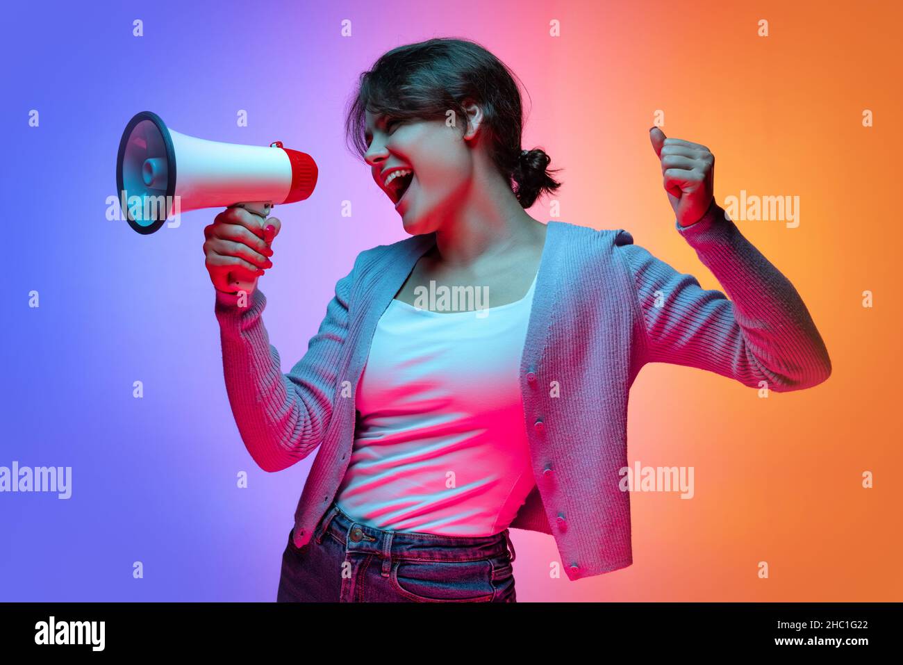 Excited young beautiful girl in warm cardigan shouting at megaphone ...