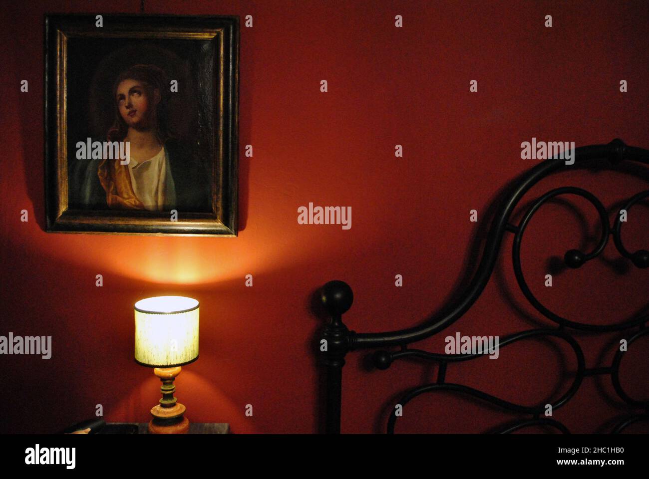 Room with amaranth-colored walls with a bed with wrought iron headboard ...