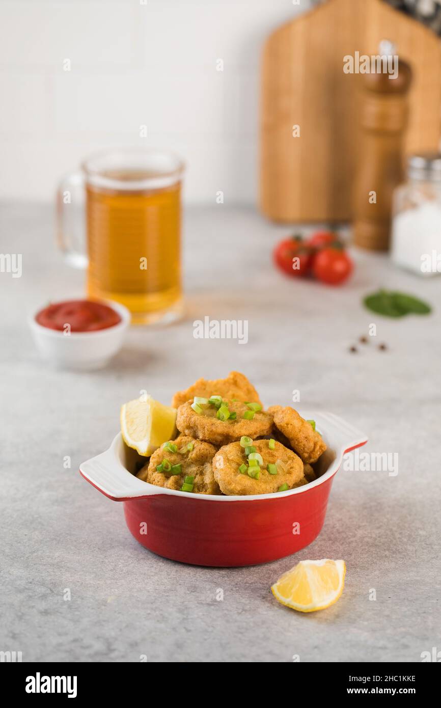 Golden chicken nuggets in a red bowl, sprinkled with green onions and a ...