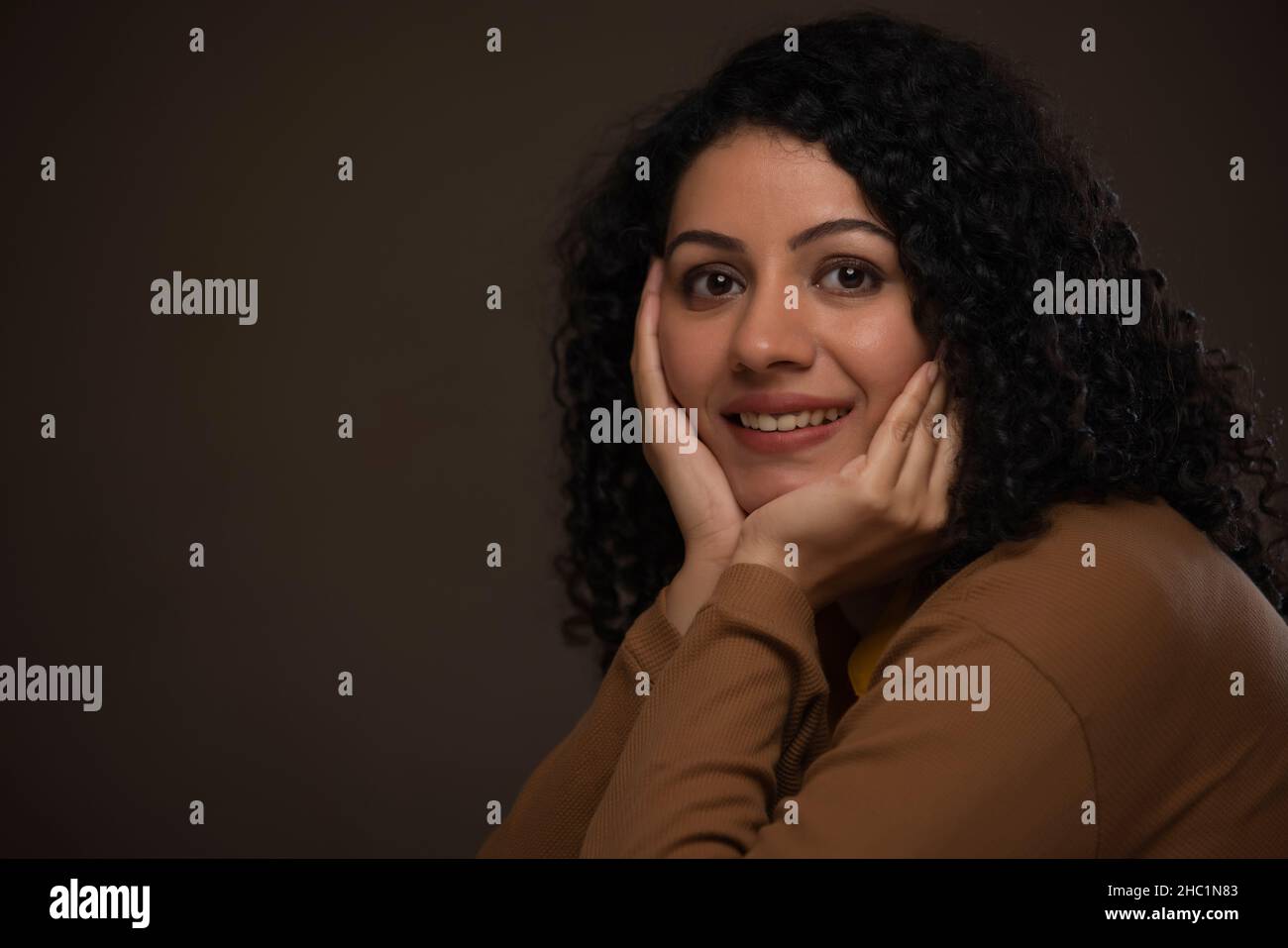 Close-up portrait of a woman with hands on cheek looking at camera ...