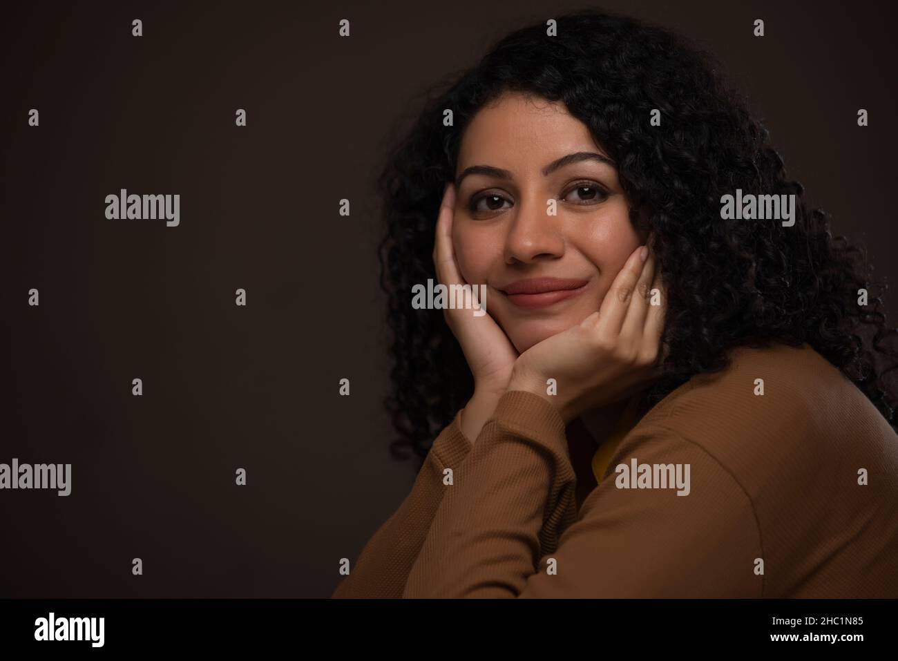 Close-up portrait of a woman with hands on cheek looking at camera ...