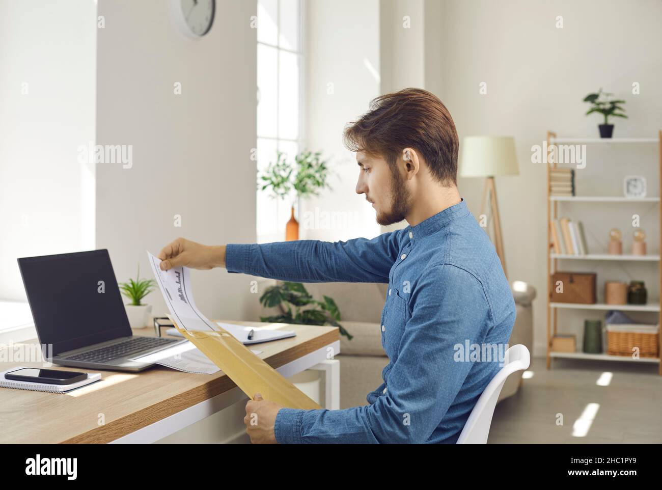 Serious young man opens envelope with business documents that he got by ...