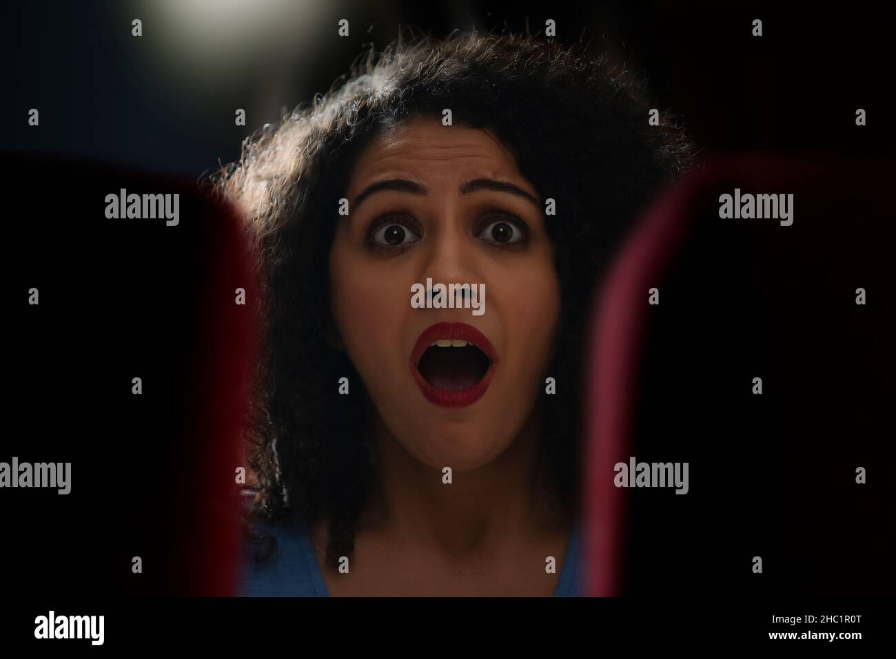 Portrait of a shocked and surprised woman while watching horror movie ...