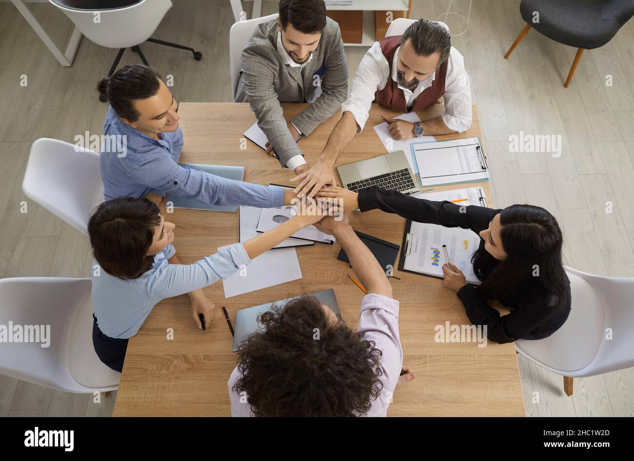 Team of business people join their hands sitting around office table in ...