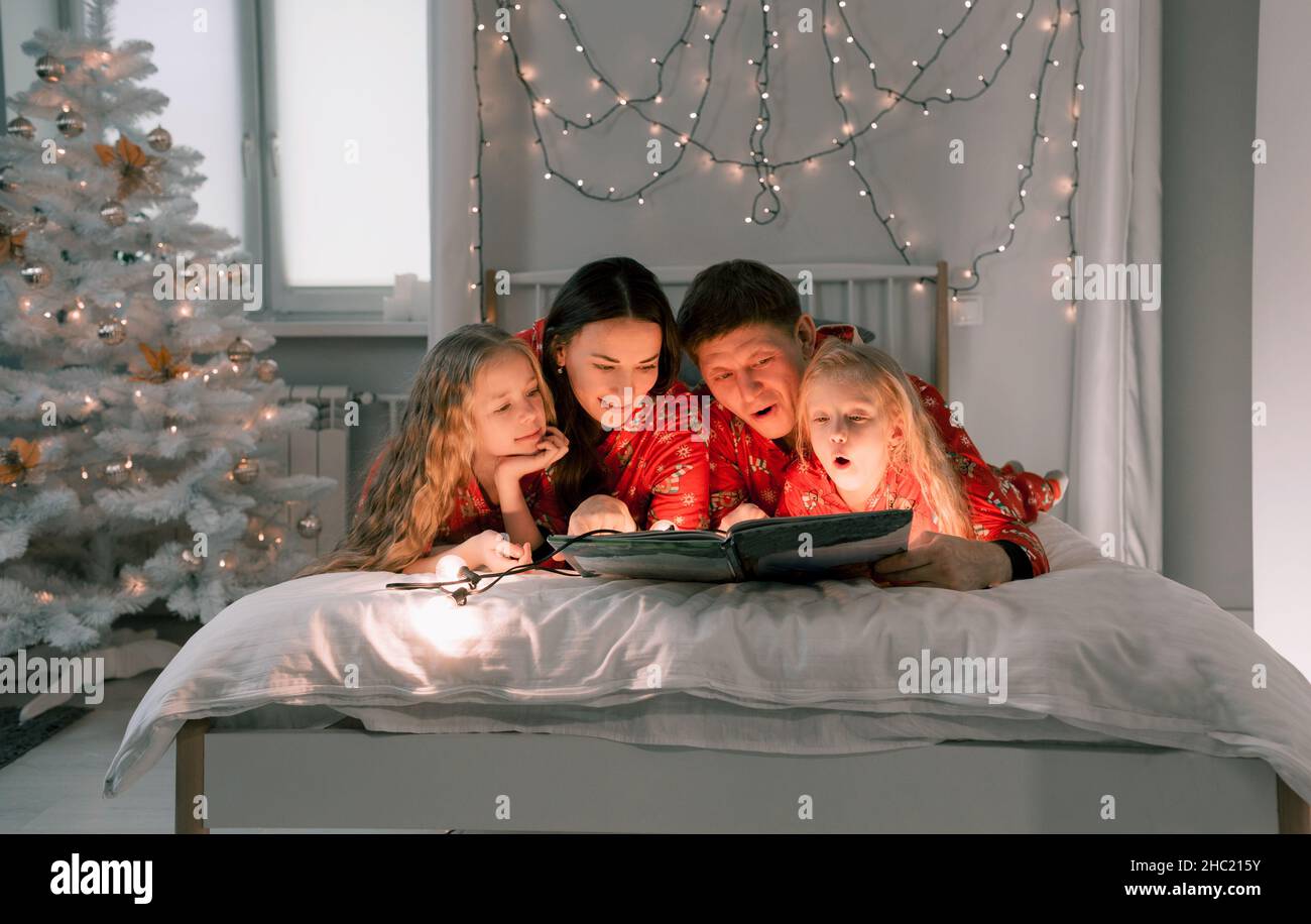 A happy family in red Christmas pajamas reading a book lying in a cozy ...