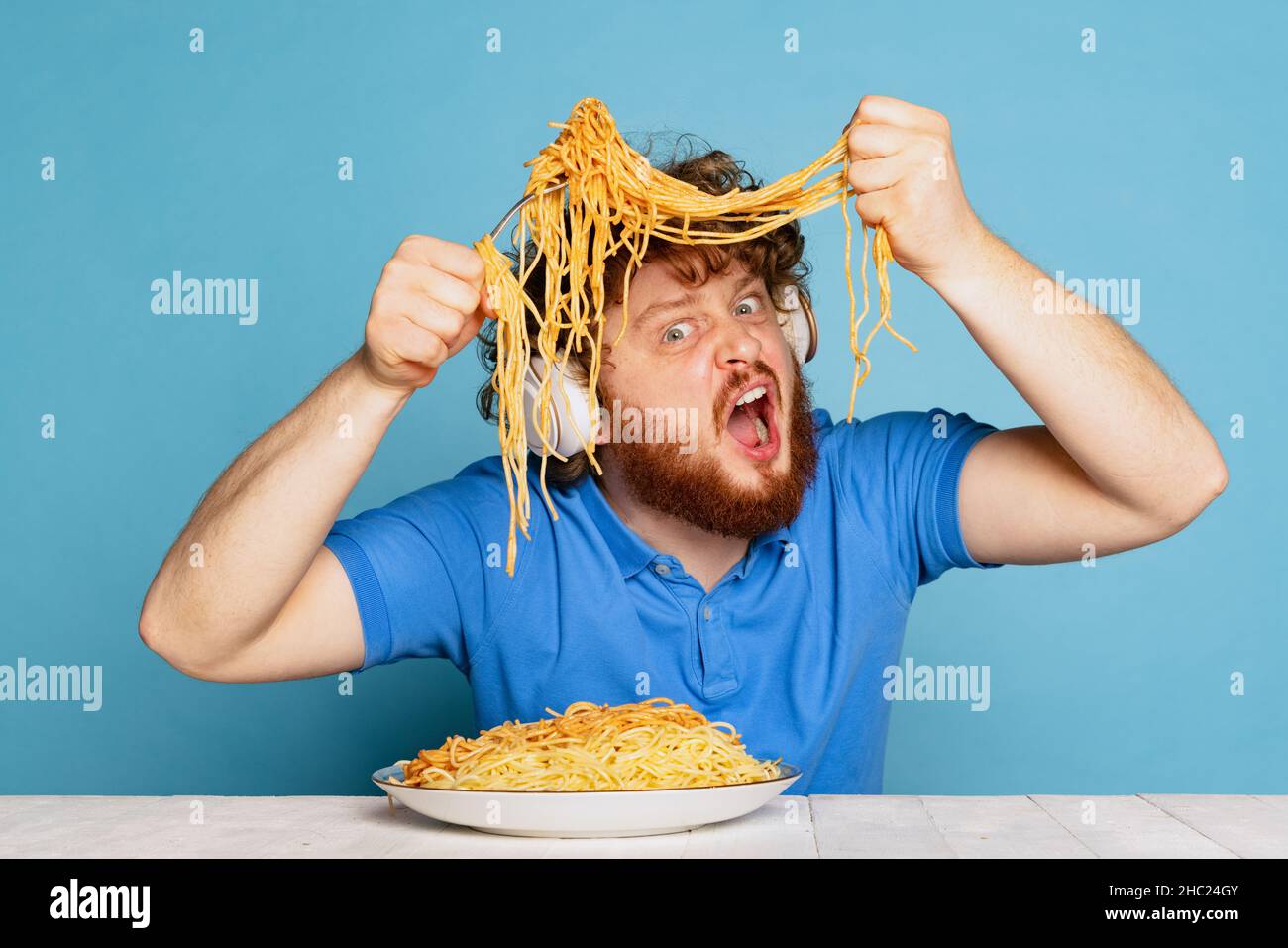 Crazy young hairy red-bearded man tasting large portion of noodles ...