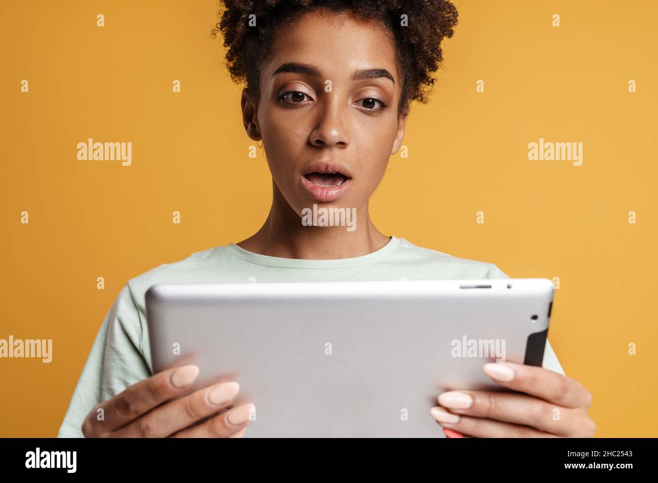 Young black woman expressing surprise while using tablet computer ...
