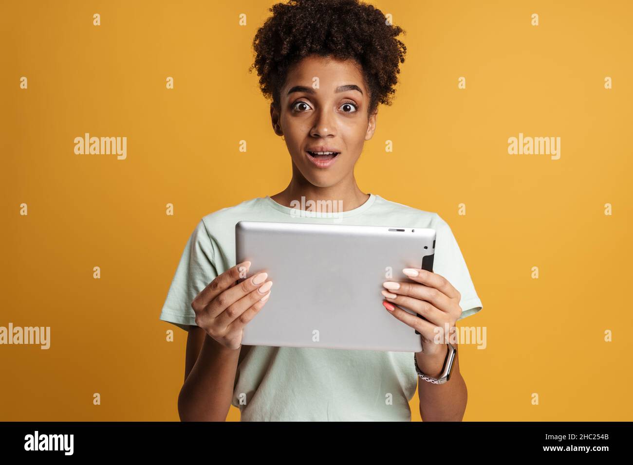 Young black woman expressing surprise while using tablet computer ...