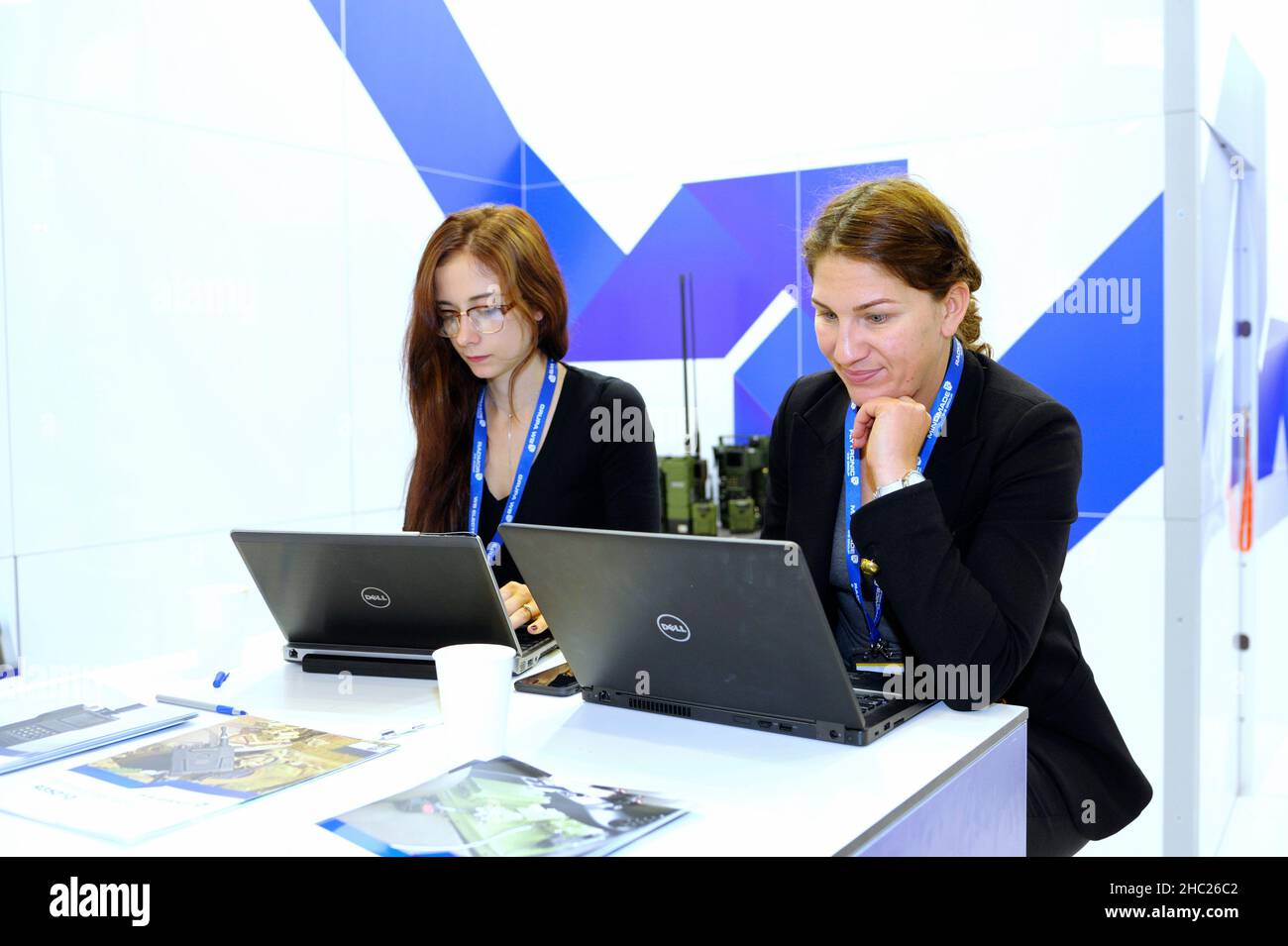 Two smiling female office workers sitting in front of laptops and work ...