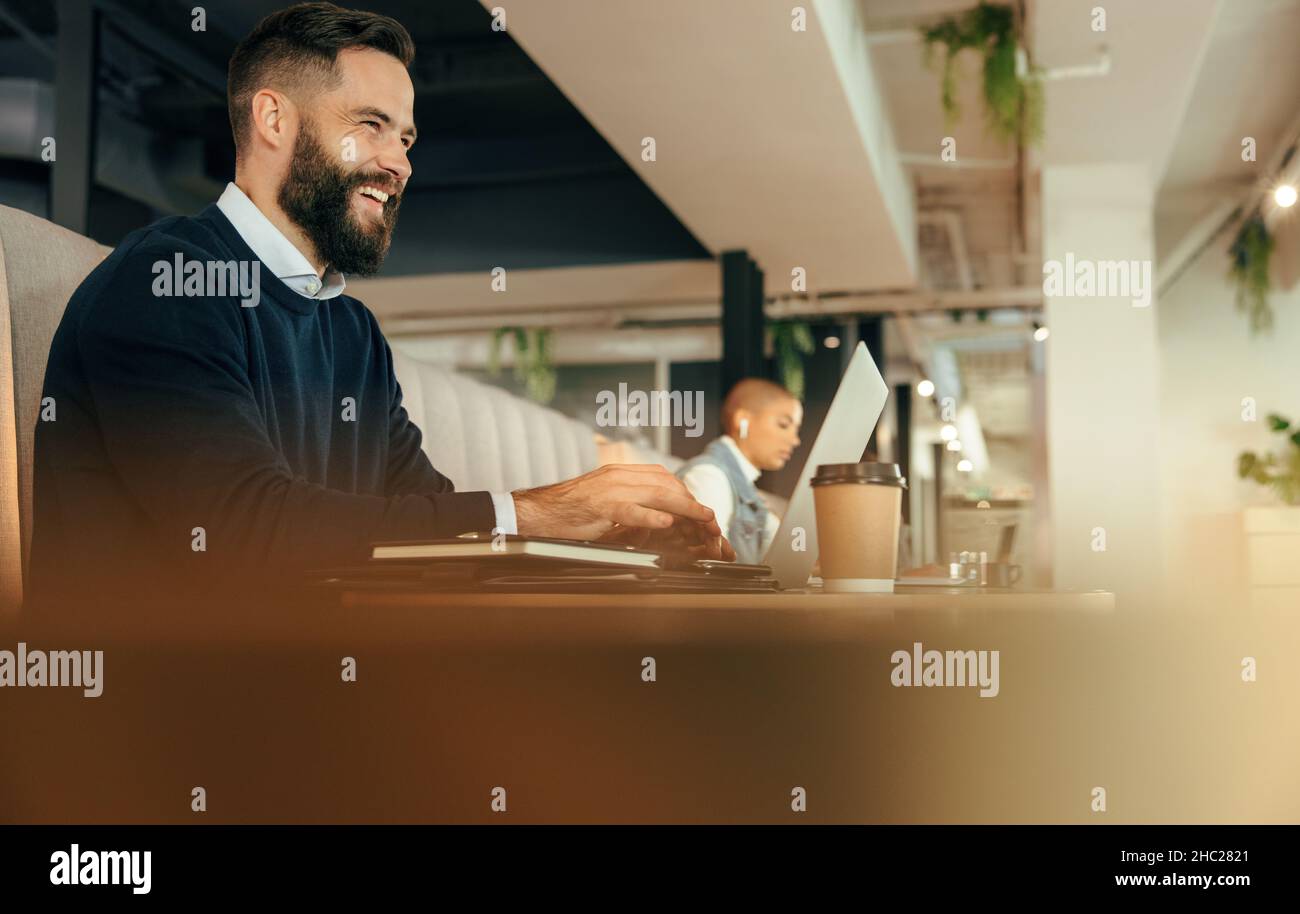 Happy young businessman working on his laptop in a co-working space ...